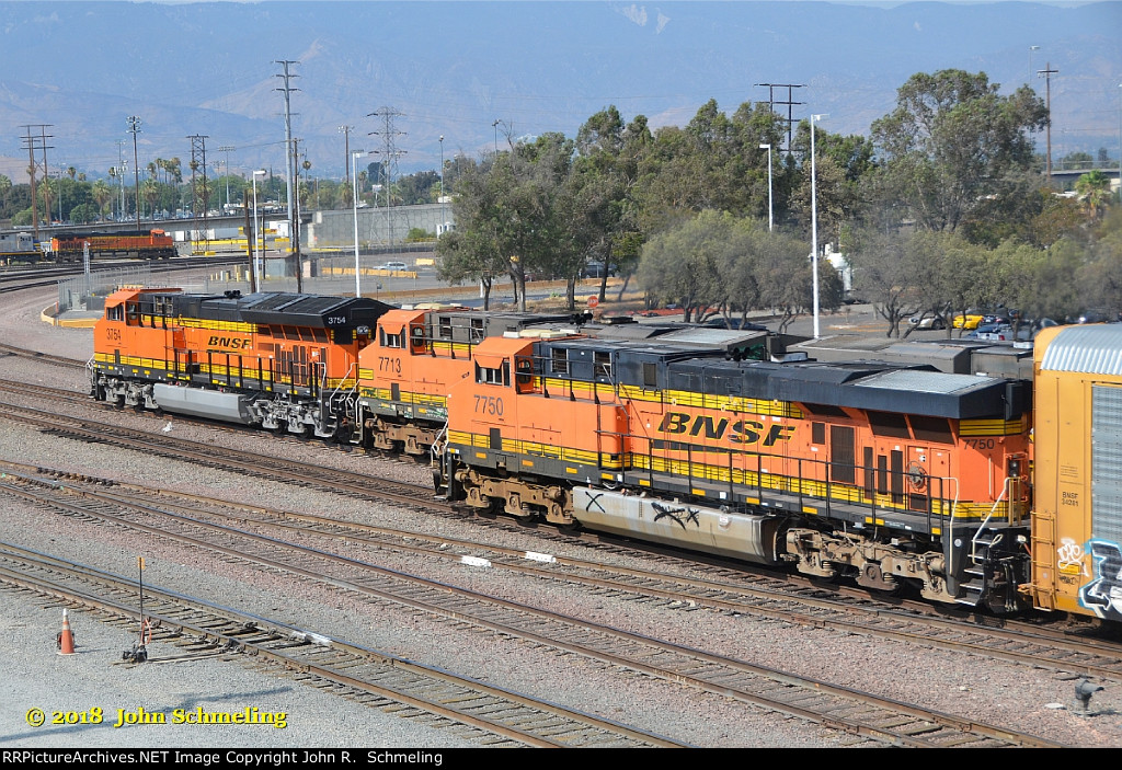 A new BNSF ET44C4 3754 leads a eastbound manifest past a waiting auto-rack train with DPU BNSF ...